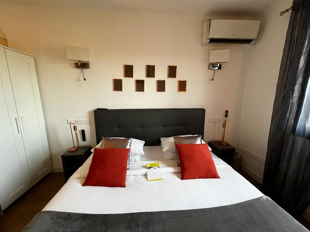Quarto de hotel com uma cama grande, duas mesas de cabeceira, um guarda-roupa e um ar condicionado fixado na parede.