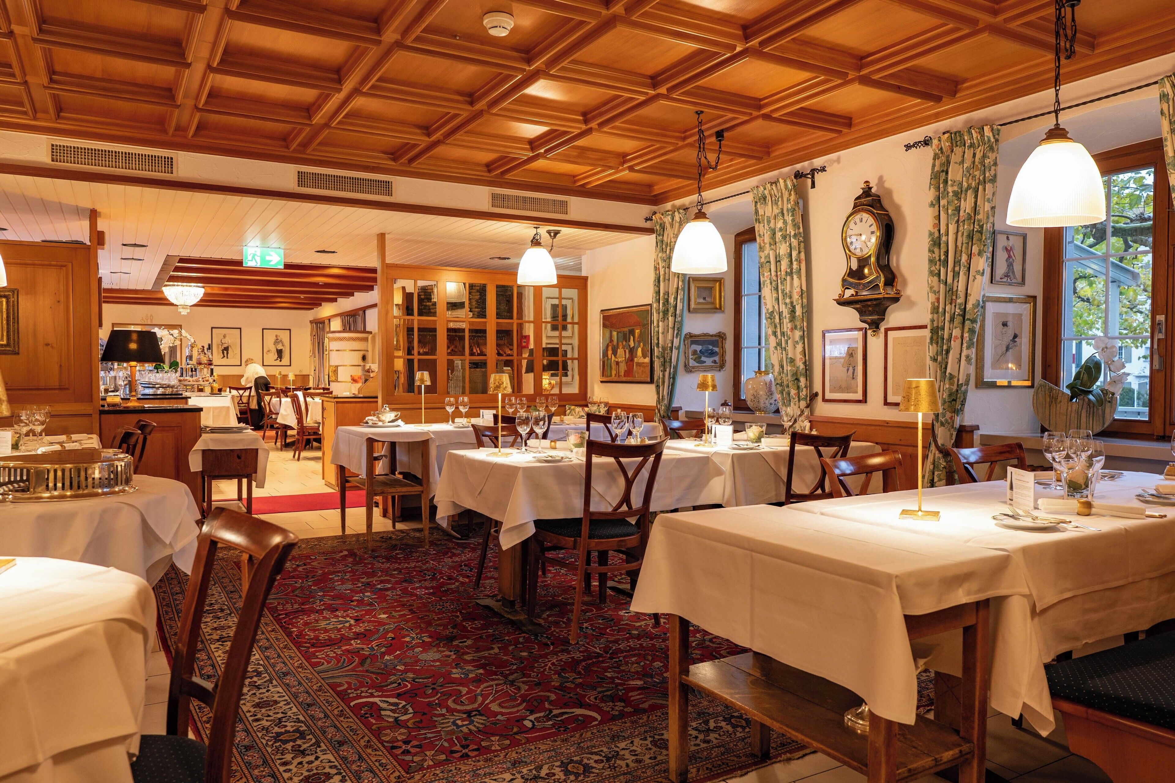 Um restaurante com vigas de madeira no teto, toalhas de mesa brancas e um tapete vermelho estampado.