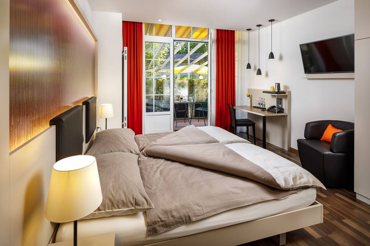 Quarto de hotel moderno com uma cama, uma escrivaninha, uma TV e vista para o exterior.
