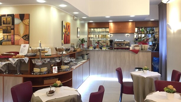 Restaurante com área de bar, buffet com diversos pratos e mesas com cadeiras.