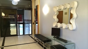 Um hall de hotel com balcão de recepção, espelho moderno e divisória de vidro.