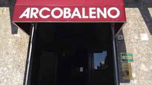 A entrada do Hotel Arcobaleno, com toldo vermelho e placa indicando que é um hotel 3 estrelas.
