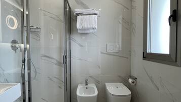 Uma casa de banho moderna com chuveiro em cabine de vidro, um bidé e uma sanita.