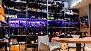 Uma área de bar com prateleiras cheias de garrafas de vinho, uma mesa de madeira e duas cadeiras.