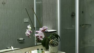 Casa de banho com lavatório, espelho, chuveiro e uma orquídea em vaso.
