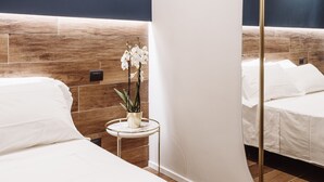 Quarto de hotel moderno com uma cama grande, uma mesinha de cabeceira com um vaso de flores e um espelho com moldura de madeira.