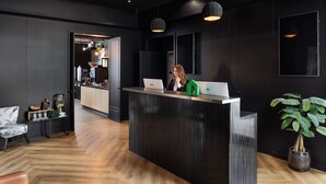 Uma área de recepção moderna com piso de madeira escura, balcão de atendimento com um laptop e uma decoração em formato de casa verde.