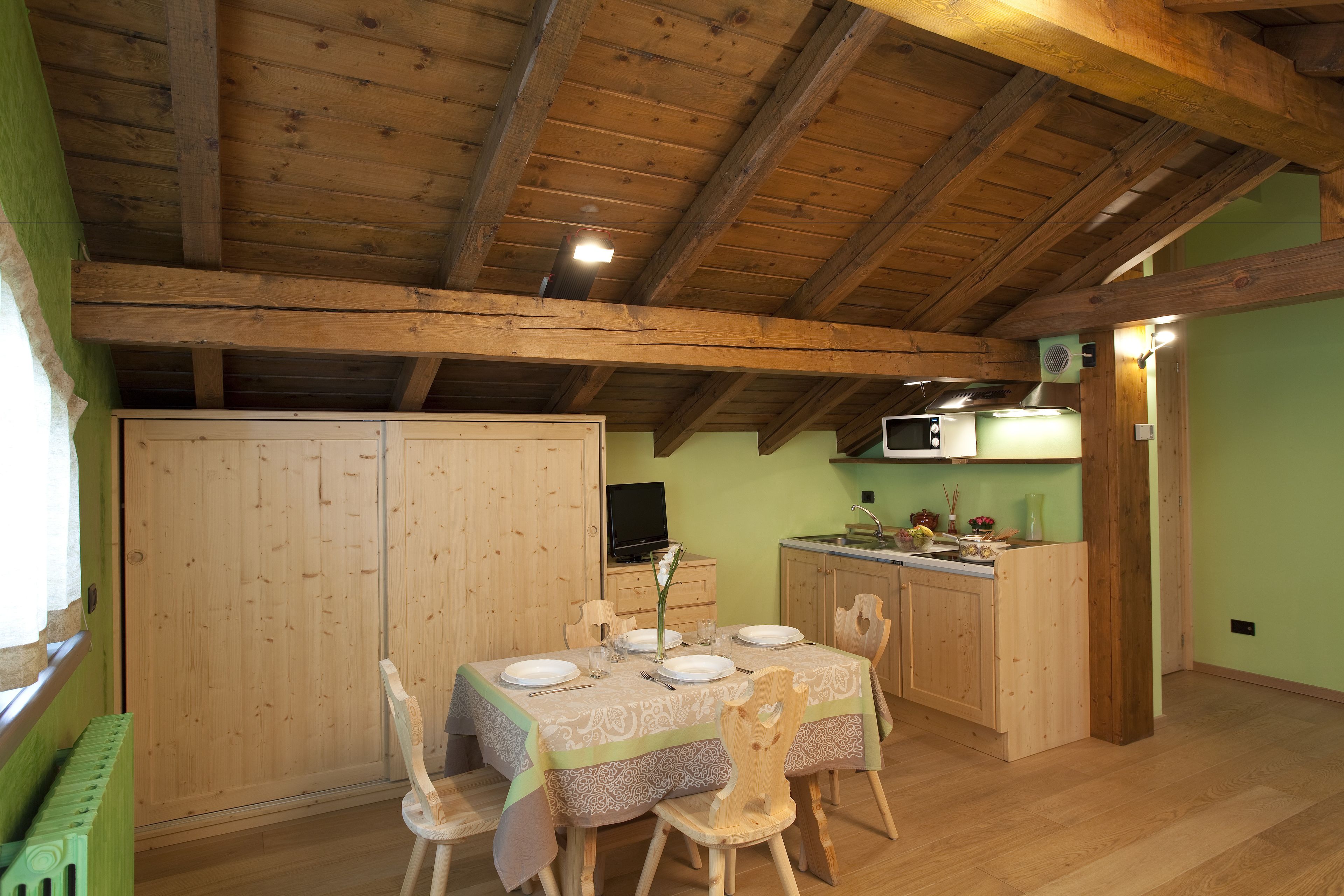 Uma área de refeições de madeira com uma mesa posta para quatro pessoas, um armário de madeira e uma cozinha compacta ao fundo.