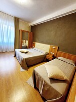 Quarto de hotel com duas camas, piso de madeira, um espelho grande e uma janela com cortinas.