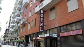 Um hotel com uma placa chamativa, uma loja com persiana fechada e um carro estacionado.