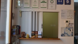 Uma área de recepção com quadros de certificados, um mural com papéis e uma janela com persianas.