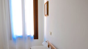 Quarto com duas camas, uma cabeceira de madeira, uma janela com cortinas leves e uma luminária fixada na parede.