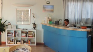 Uma área de recepção com balcão azul, estante cheia de livros, mapa emoldurado e um vaso de planta.