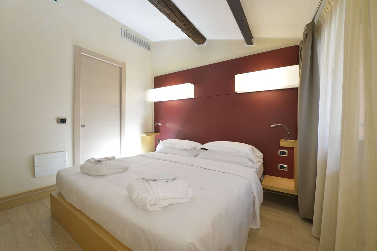 Quarto de hotel com cama, mesas de cabeceira e cabeceira com iluminação embutida.