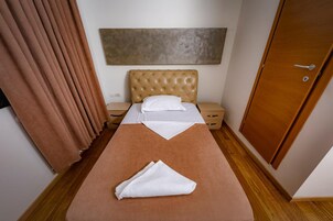 Cama bem arrumada com cabeceira marrom, travesseiro branco e toalha branca dobrada sobre a cama.