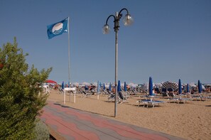Uma praia com fileiras de espreguiçadeiras e guarda-sóis, uma bandeira e um poste de luz.