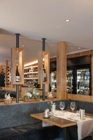 Um restaurante com balcão de madeira, assentos acolchoados e garrafas de vinho expostas em prateleiras.