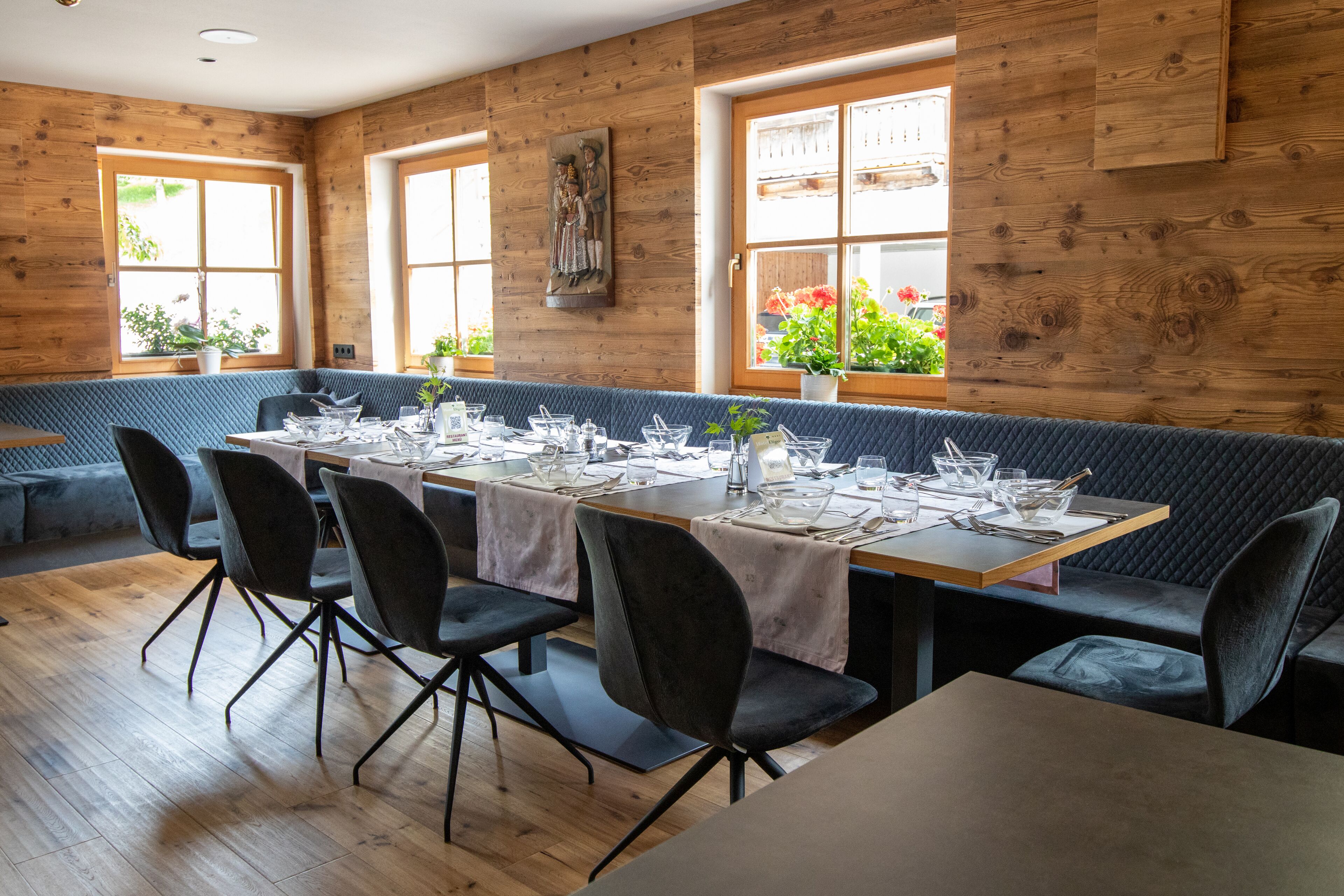 Um restaurante com paredes de madeira, janelas amplas e uma variedade de opções de assento, incluindo mesas e bancos.