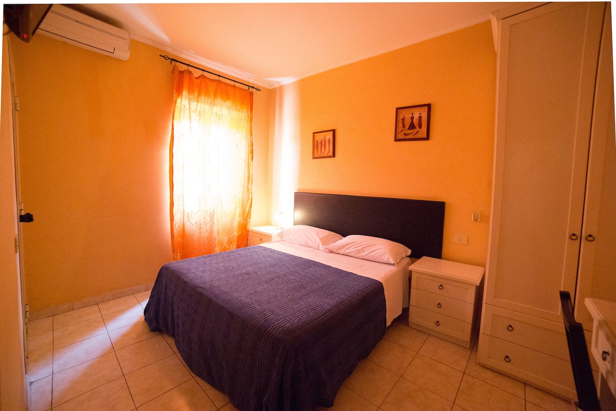 Quarto com cama, mesas de cabeceira, cômoda e guarda-roupa.