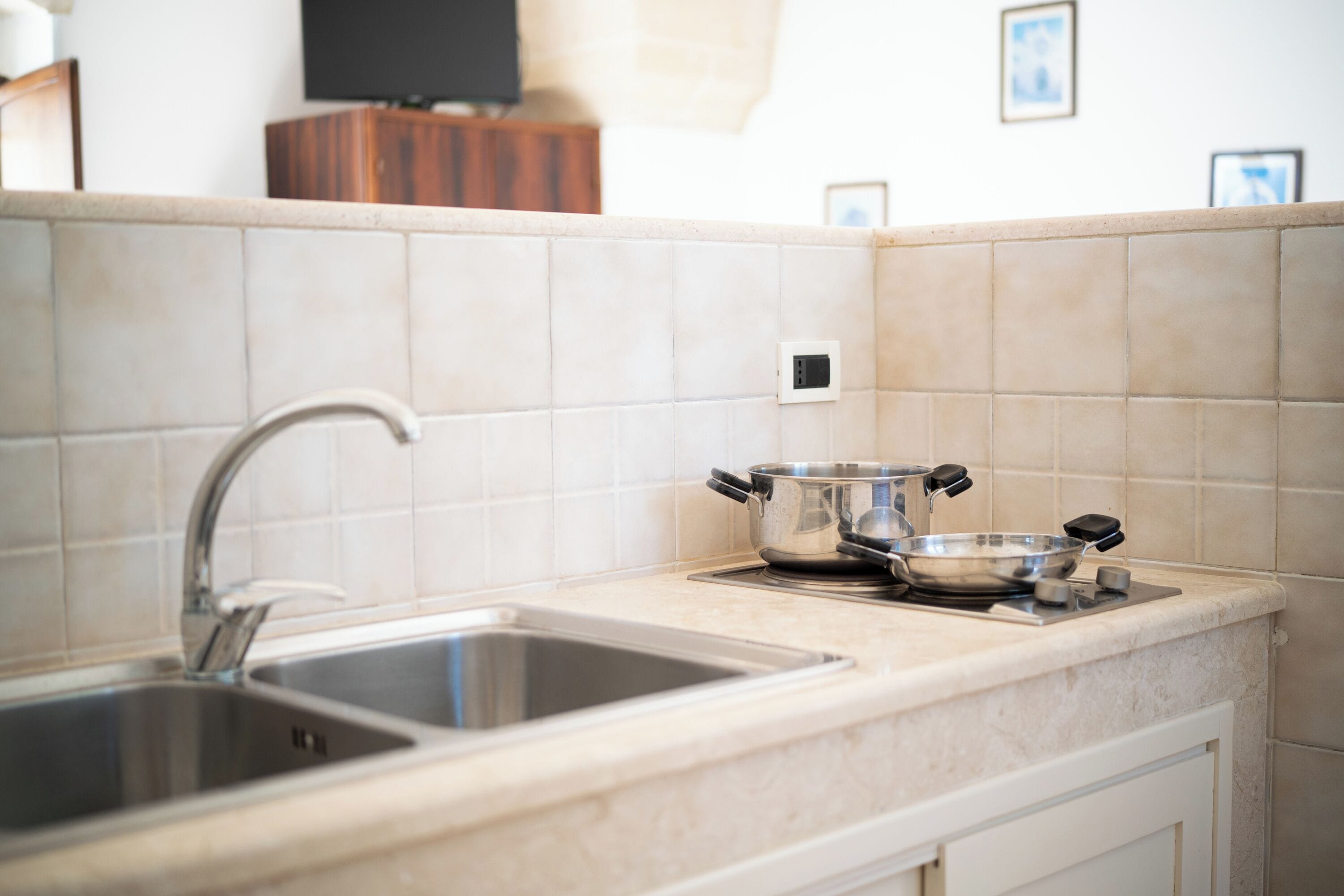 Cozinha com pia de aço inoxidável, fogão e painel de azulejos.