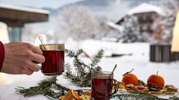 Duas chávenas de bebida vermelha sobre uma mesa coberta de neve, com uma decoração festiva incluindo bolachas e laranjas.