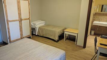 Quarto com cama, mesa de cabeceira pequena, cadeira, guarda-roupa e banheiro com pia e espelho.