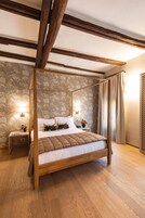 Uma cama de dossel com estrutura de madeira e colcha acolchoada, em um quarto com piso de madeira e papel de parede estampado com flores.