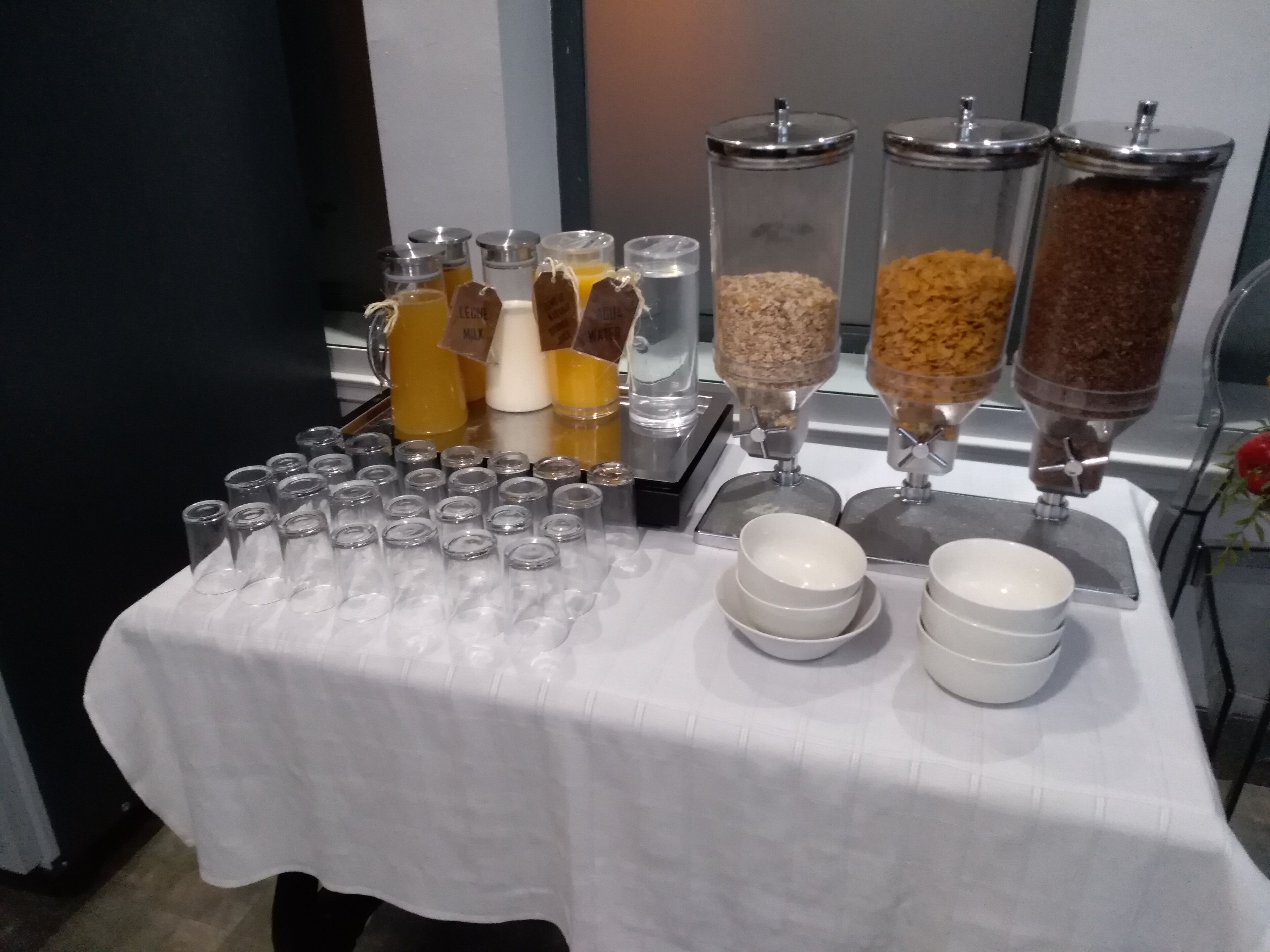 Uma mesa de buffet com diversos dispensadores de alimentos, incluindo leite, água e cereais.