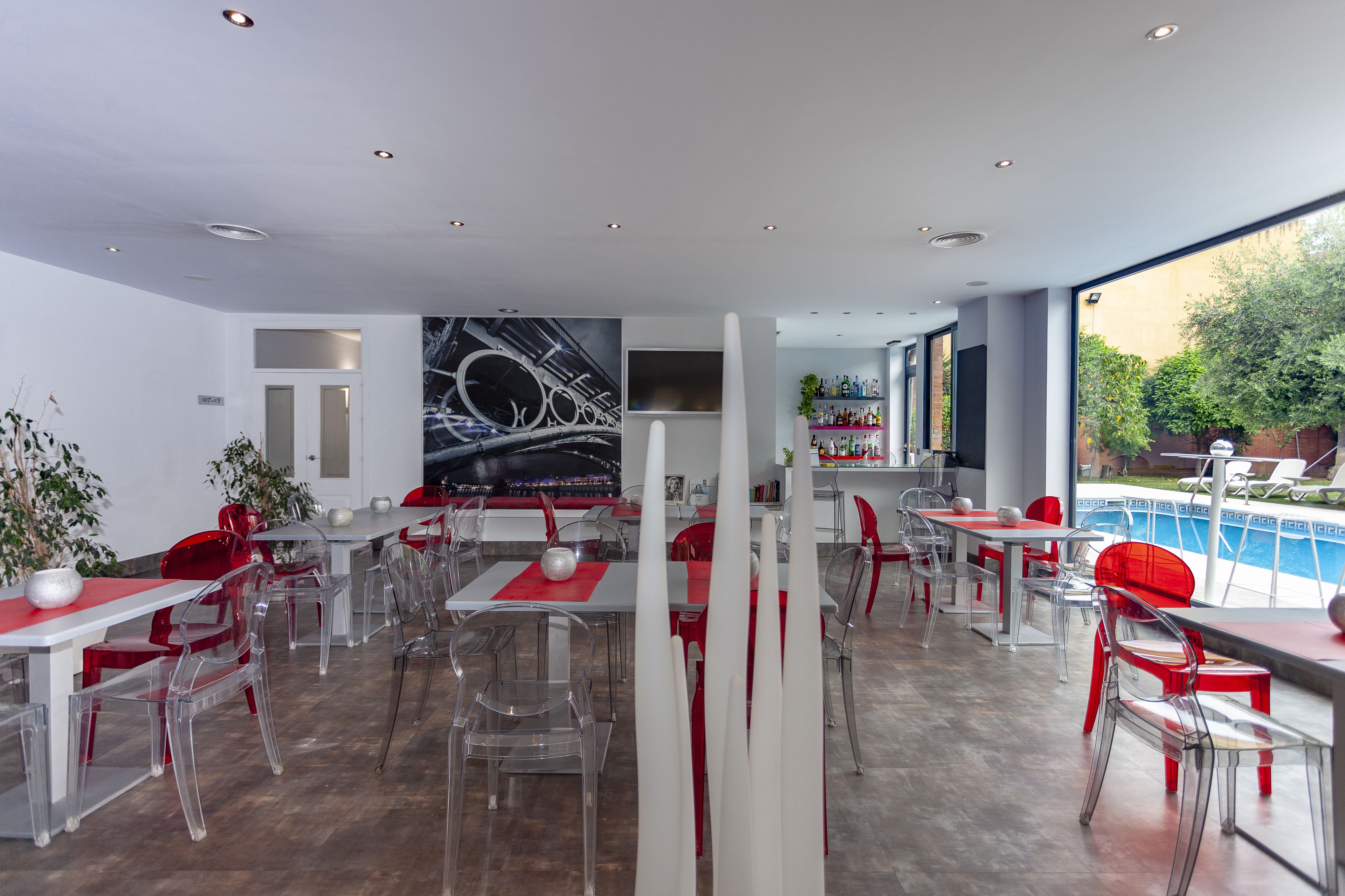 Um restaurante moderno com cadeiras e mesas de vidro transparente, vista para a piscina e uma grande pintura abstrata na parede.