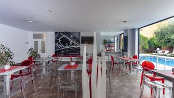 Um restaurante moderno com cadeiras e mesas de vidro transparente, vista para a piscina e uma grande pintura abstrata na parede.