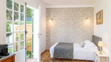 Quarto com cama, duas luzes fixadas na parede, mesa de cabeceira com abajur e janela com vista para o verde.