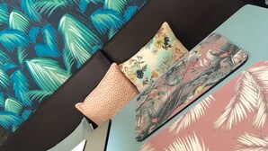 Quarto com parede estampada, cama com colcha floral e travesseiro com bolinhas.