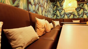 Um sofá de couro marrom com almofadas estampadas em um quarto com papel de parede de folhas tropicais.