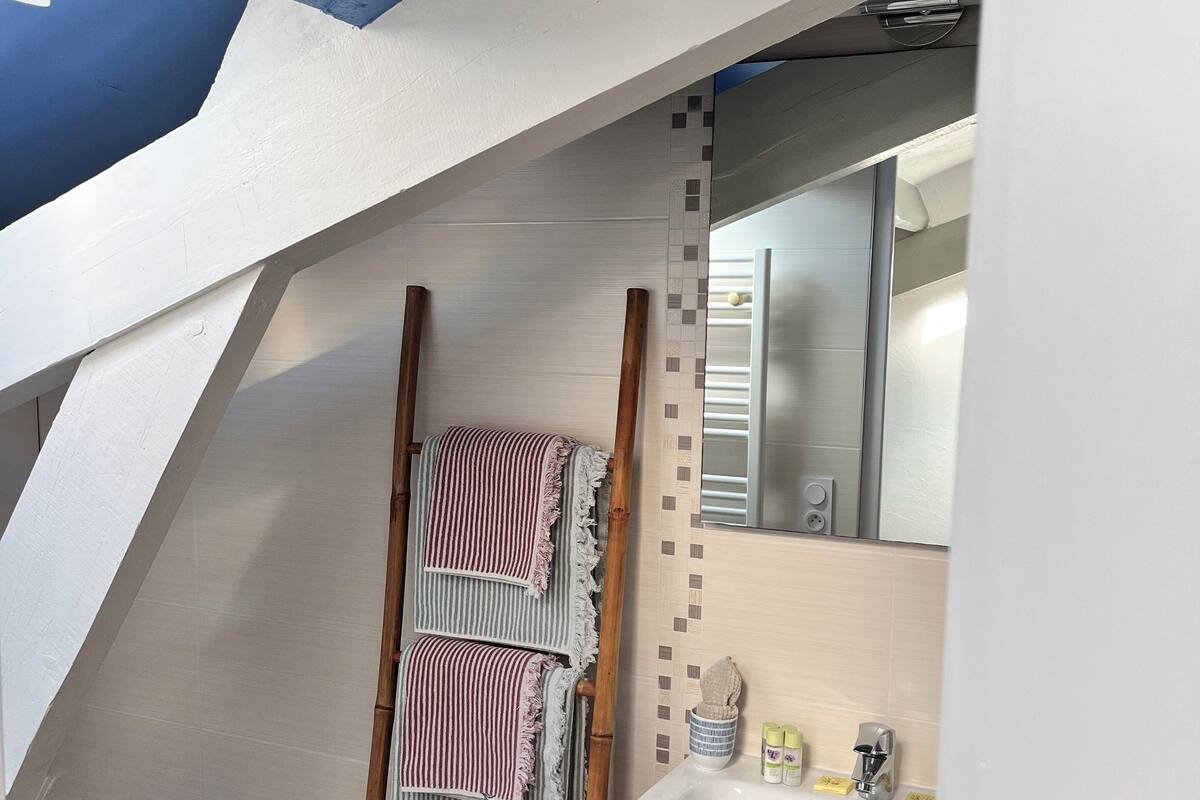 Casa de banho com lavatório branco, gavetas de madeira, espelho e toalheiro com toalhas listradas.