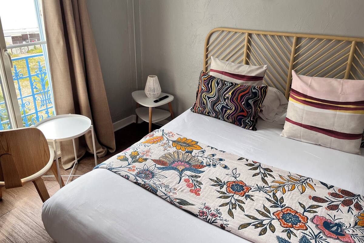 Quarto de hotel com cama, uma mesinha, uma cadeira e vista para o exterior.