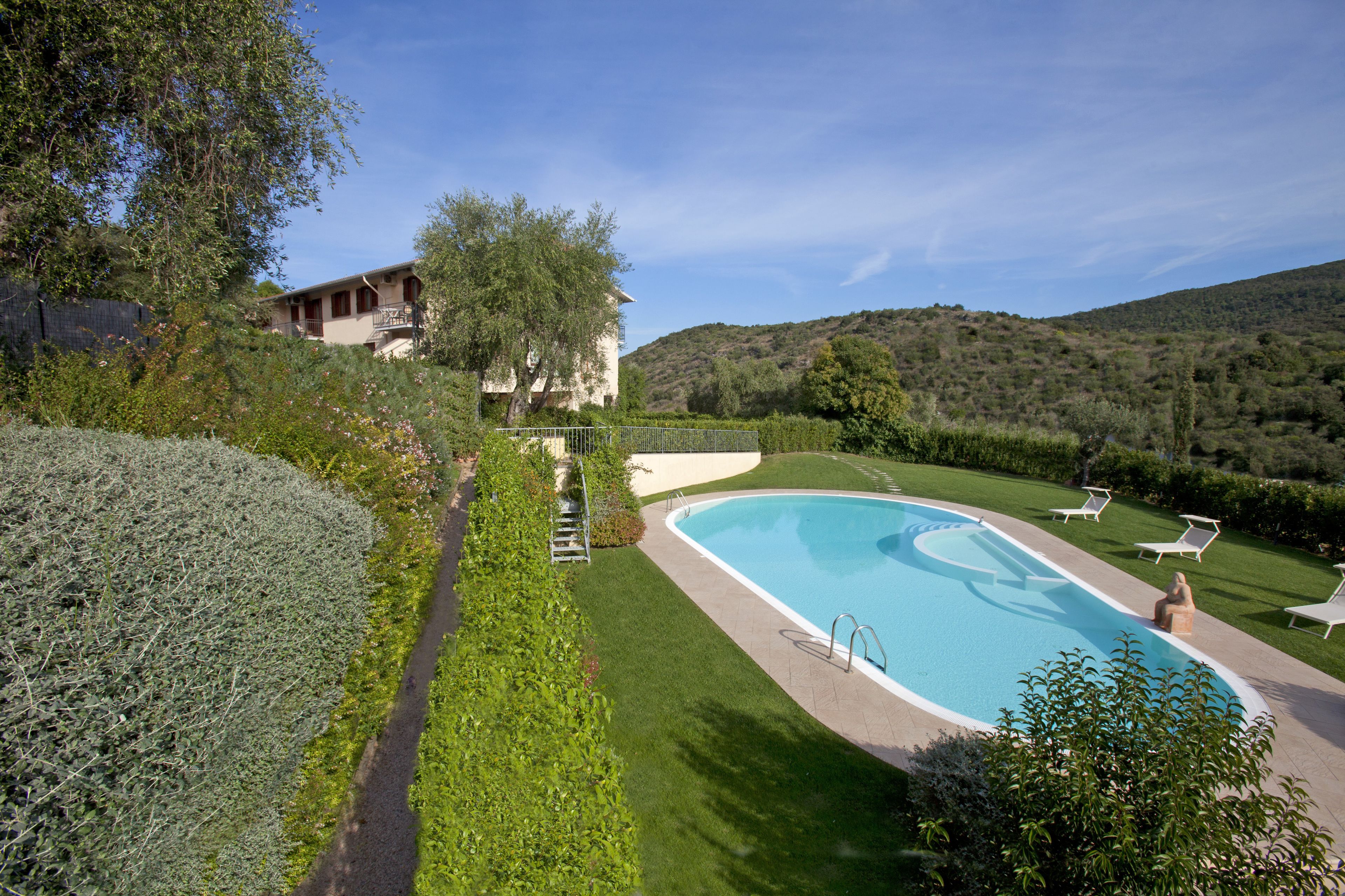 Uma piscina rodeada por um relvado bem cuidado, uma casa com varanda e uma paisagem montanhosa ao fundo.