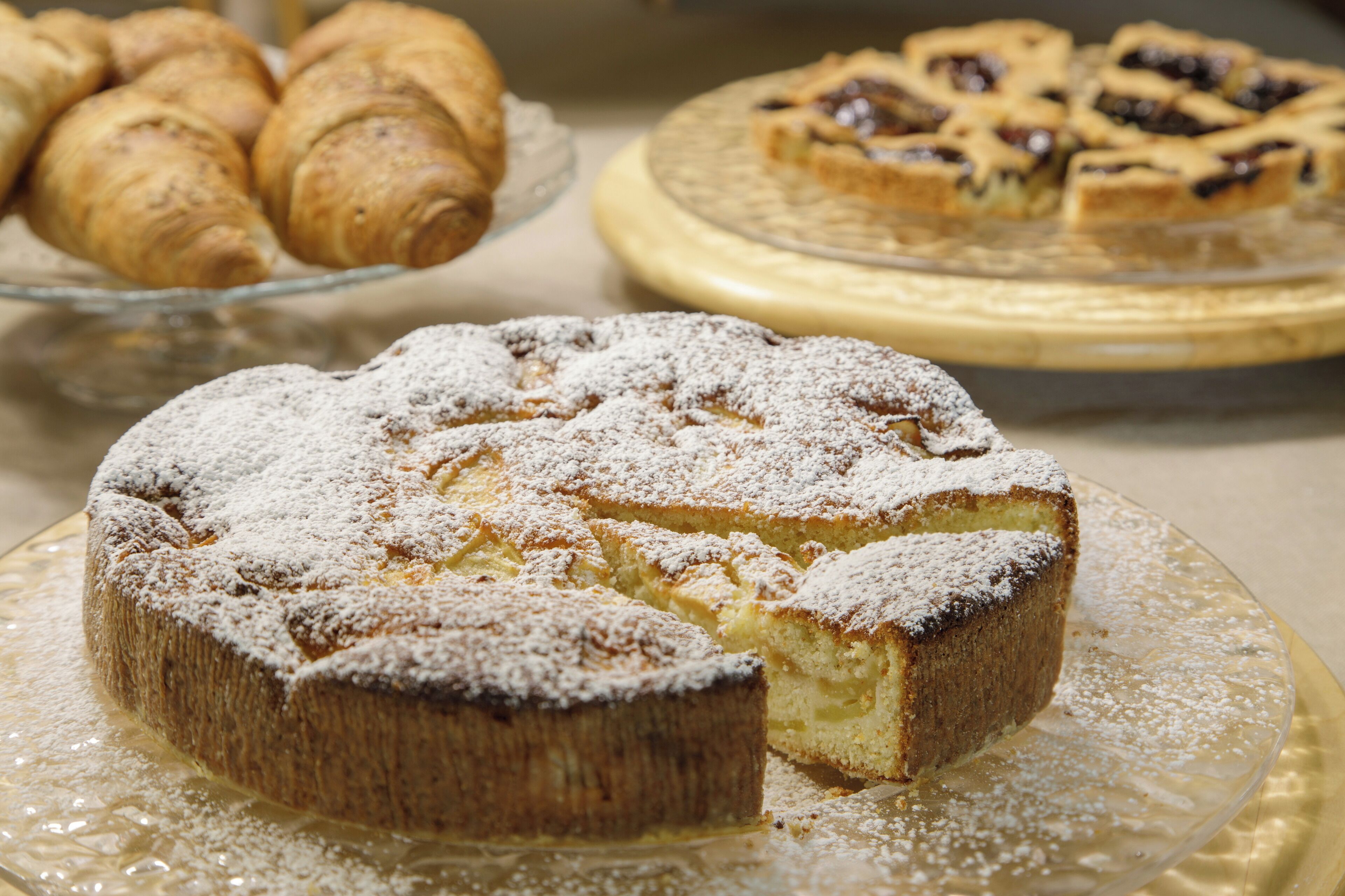 Uma mesa de sobremesas com diversos doces e bolos, incluindo um bolo polvilhado e uma torta com cobertura em treliça.