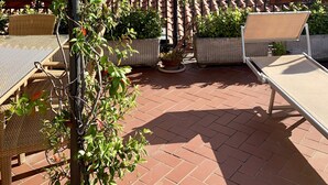 Uma área de estar ao ar livre com móveis de vime, plantas em vasos e vista para um edifício histórico com torre.