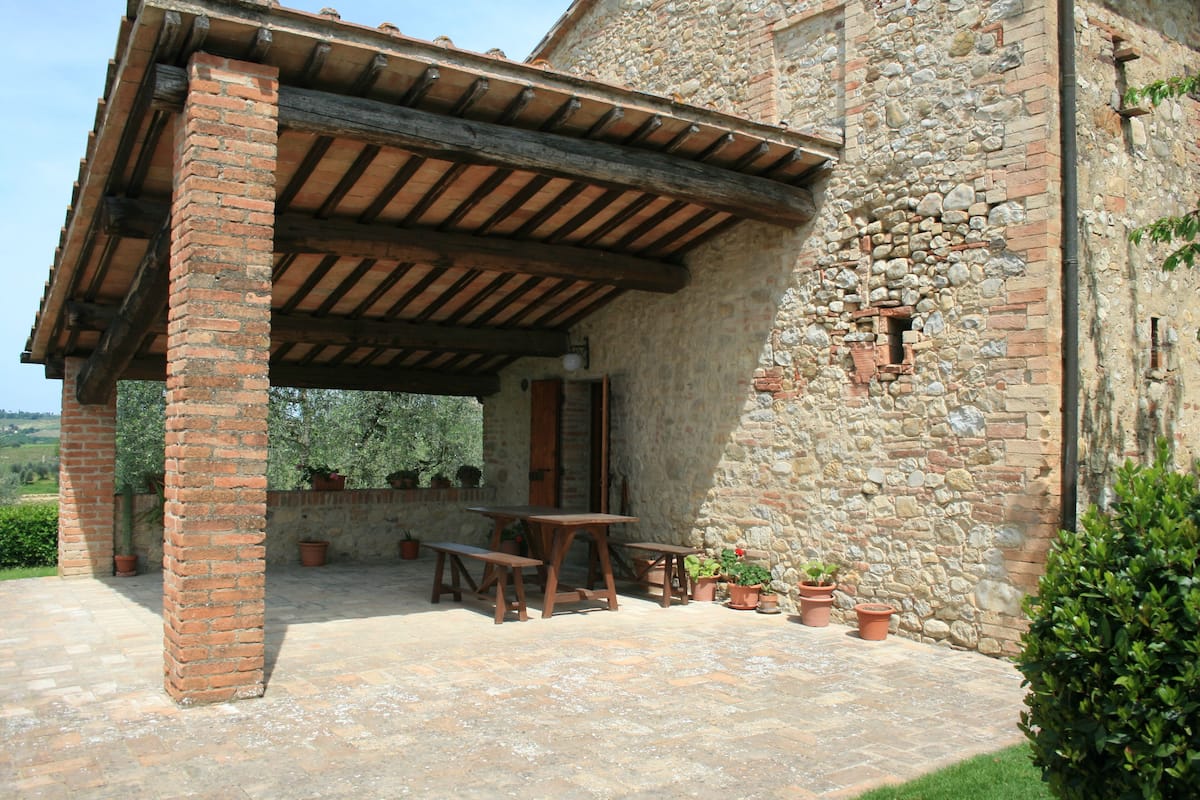 Um edifício de pedra com um alpendre coberto, com uma mesa e bancos de madeira.