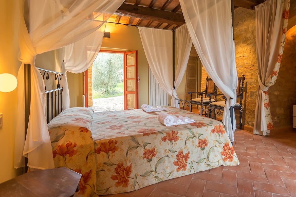 Um quarto com cama, cortinas, uma cadeira e vista para o exterior.