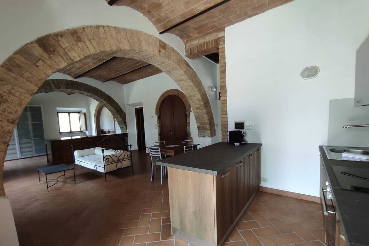 Uma cozinha espaçosa com uma ilha central, arcos de tijolos e uma área de refeições com sofá e cadeiras.