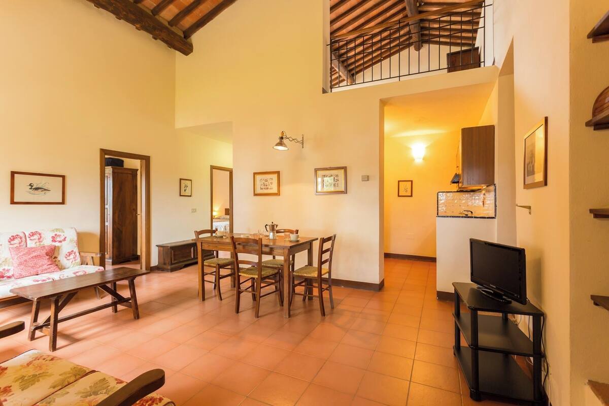 Uma sala de estar espaçosa com uma mesa de jantar, cadeiras, sofá, televisão e uma escada para um andar superior.