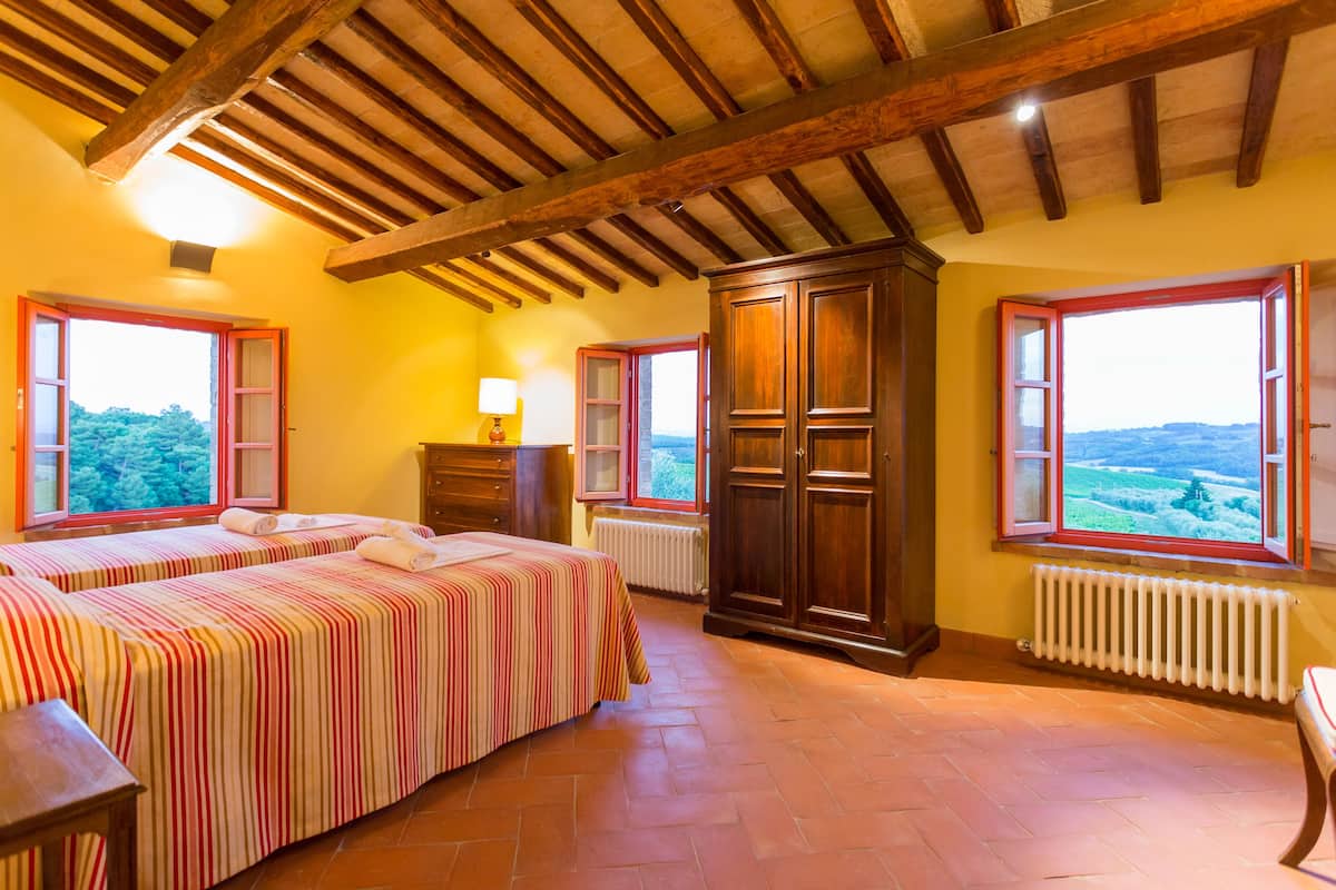 Quarto com duas camas, armários de madeira, radiador e grandes janelas com vista.