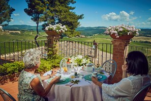 Mesa de jantar posta ao ar livre, com vista panorâmica de colinas e vinhedos.