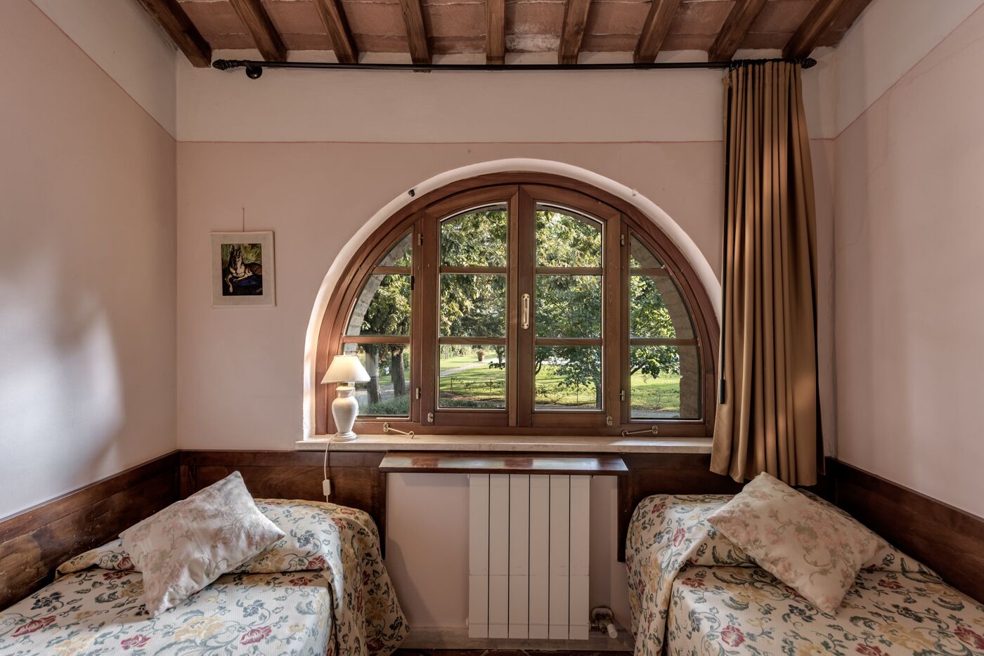 Quarto com duas camas de solteiro, um radiador, uma janela com cortinas e uma luminária.