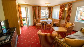 Quarto de hotel com carpete vermelho, poltronas listradas, mesa de jantar e televisão sobre um móvel de madeira.
