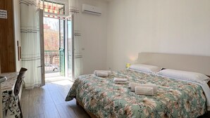 Quarto com cama, escrivaninha e cadeira. Há uma janela com cortinas e um ar condicionado na parede.