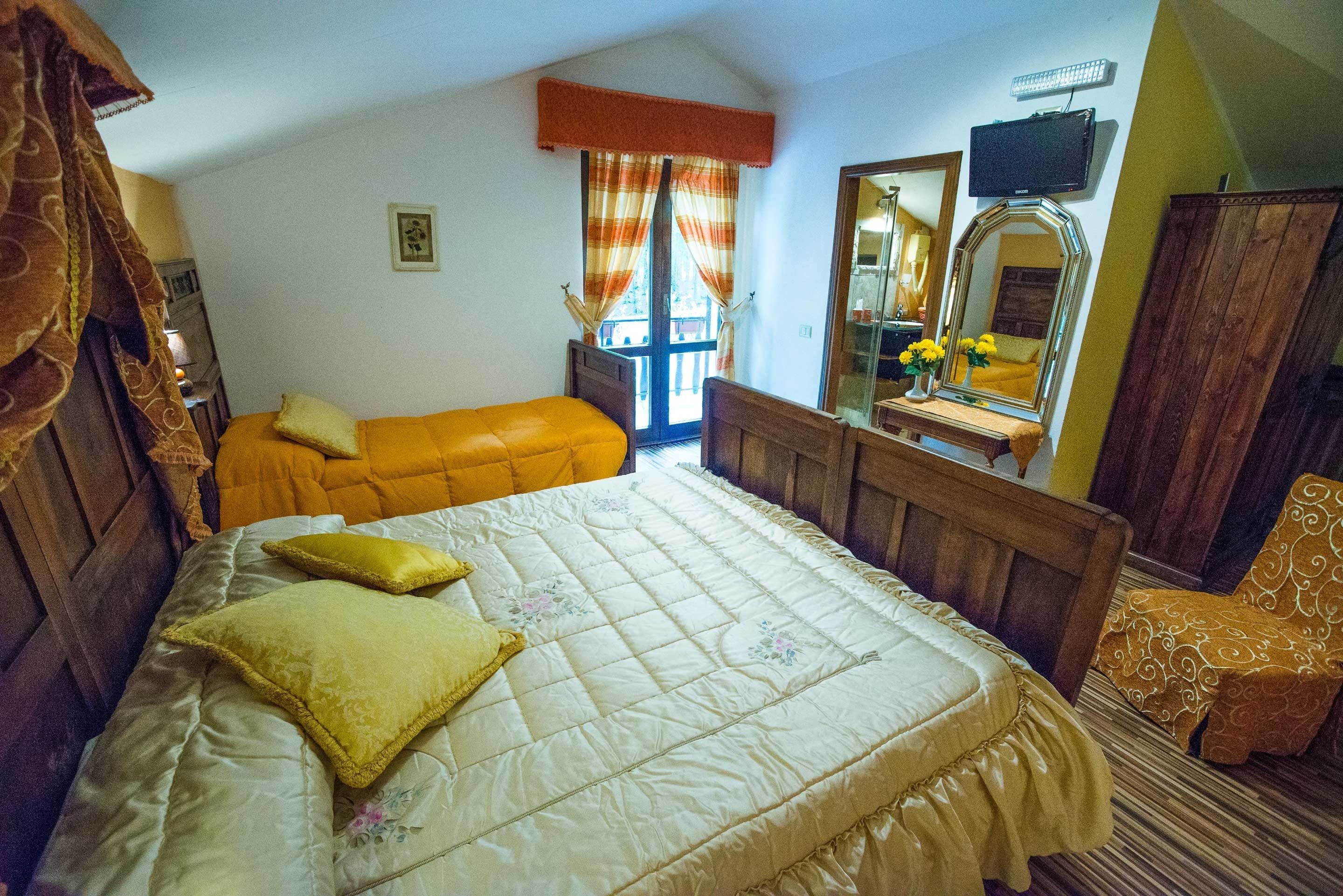 Quarto com cama grande, um sofá menor, um espelho e uma televisão.