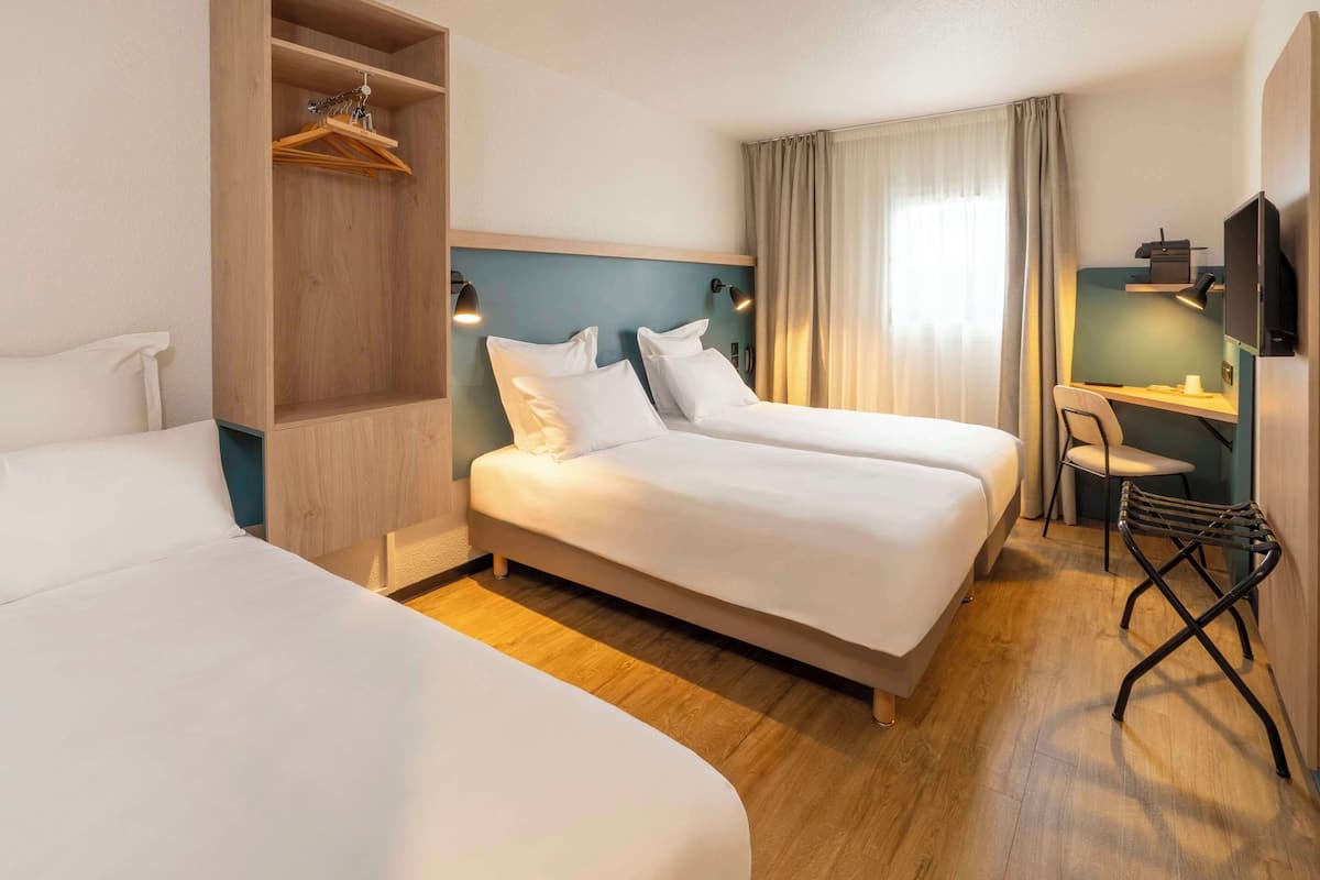 Quarto de hotel com duas camas, uma escrivaninha, uma cadeira e um guarda-roupa.