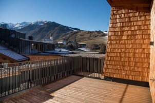 Um deck de madeira com guarda-corpo de metal, com vista para uma paisagem montanhosa com uma igreja e edifícios residenciais.